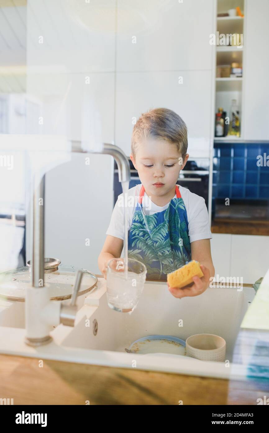 a boy in an apron washes dishes in the kitchen at home Stock Photo - Alamy
