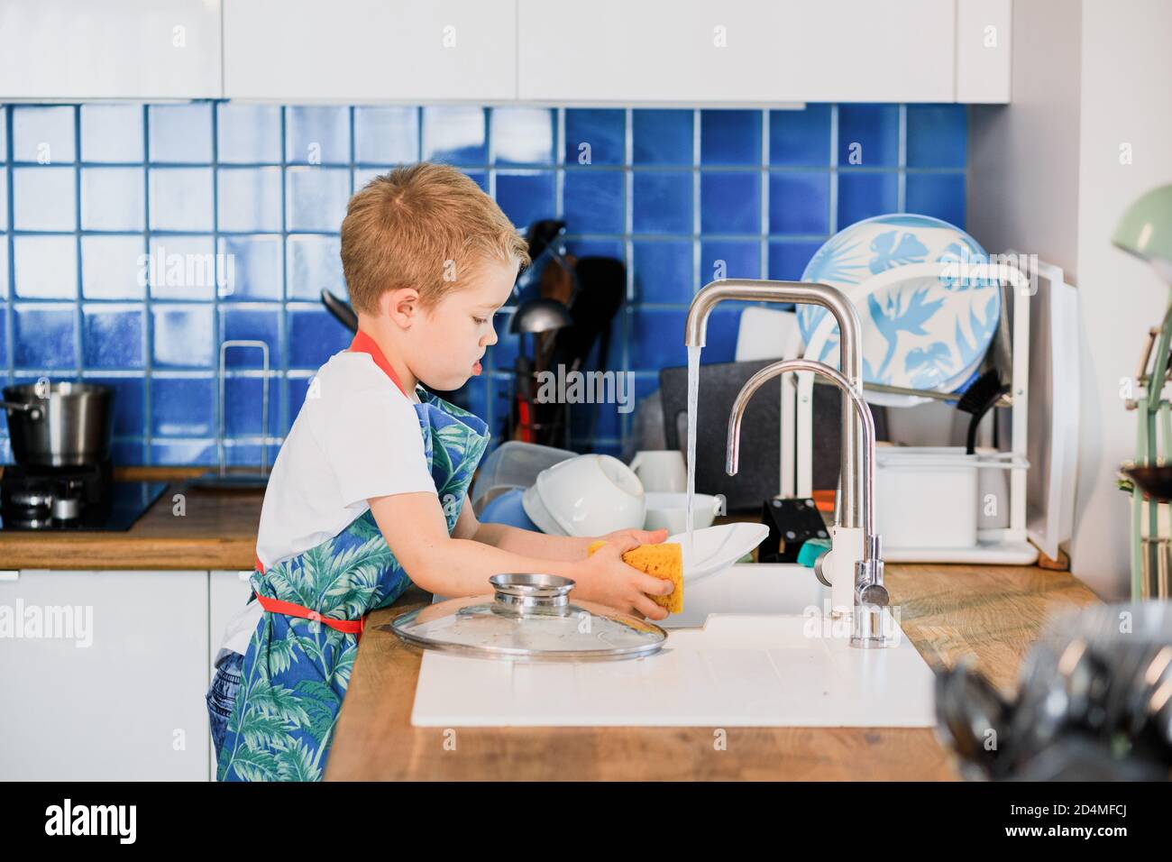 a boy in an apron washes dishes in the kitchen at home Stock Photo - Alamy
