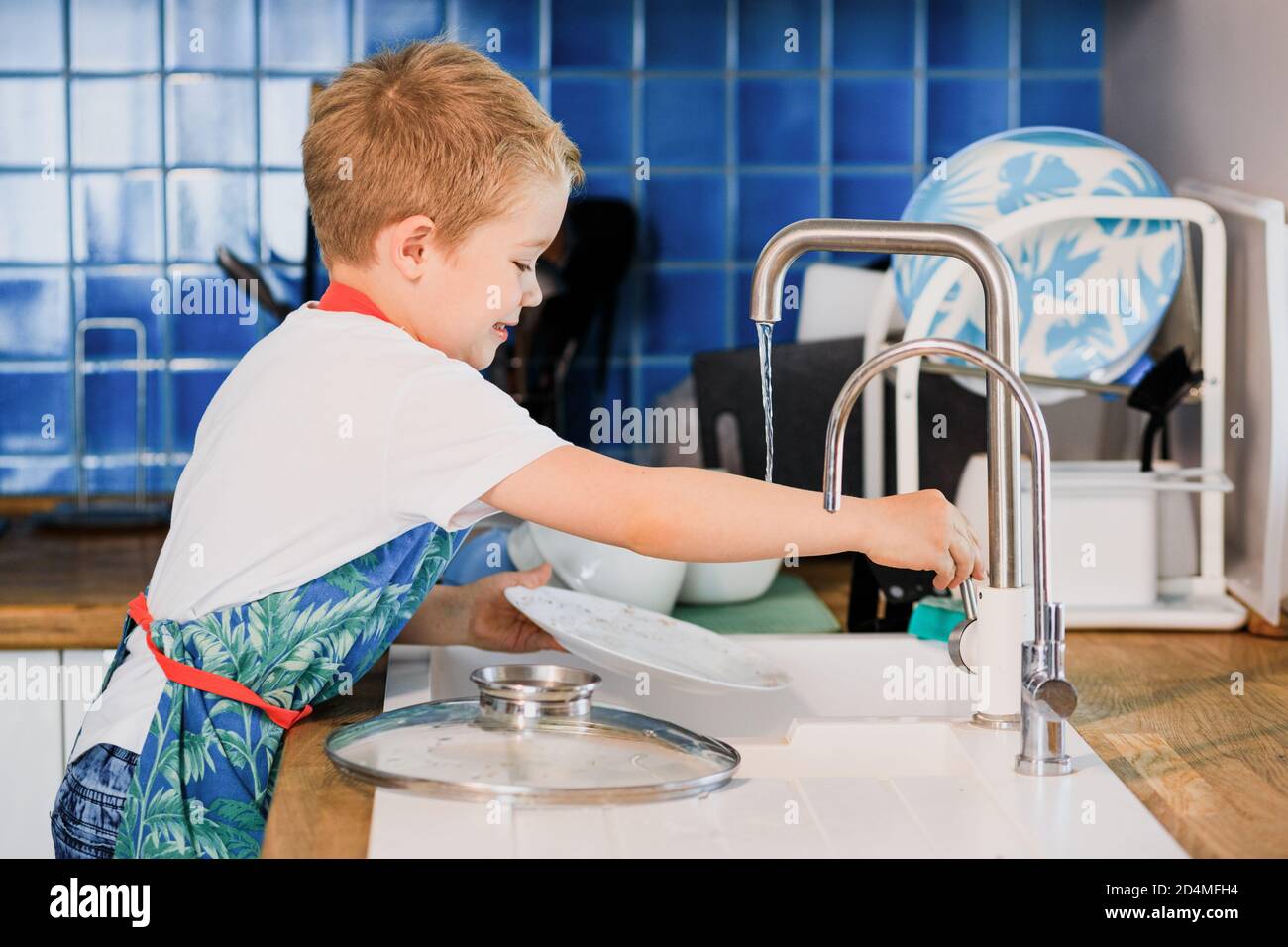 a boy in an apron washes dishes in the kitchen at home Stock Photo - Alamy