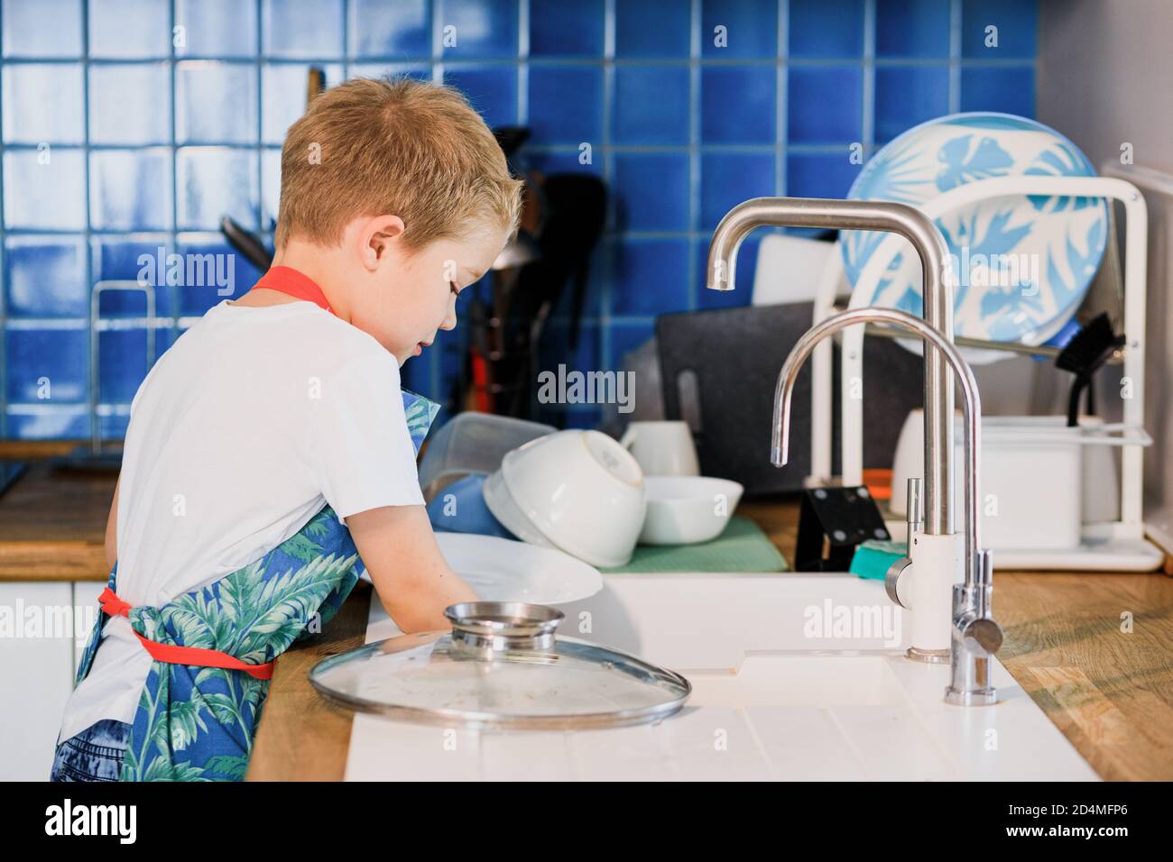 a boy in an apron washes dishes in the kitchen at home Stock Photo - Alamy