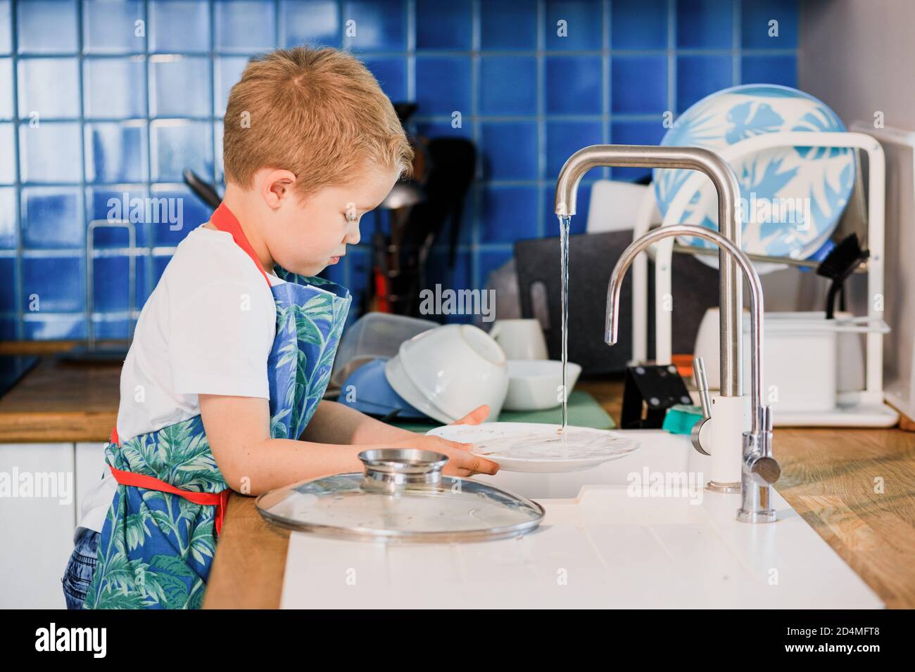 a boy in an apron washes dishes in the kitchen at home Stock Photo - Alamy
