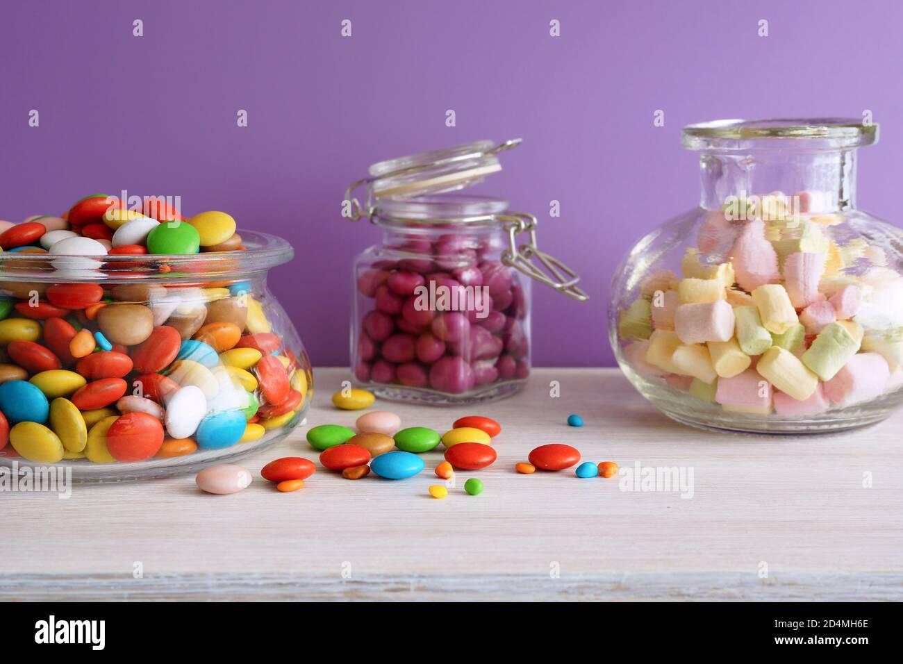 Multi-colored sweets. Candies in glass jars on a white table. Lilac ...