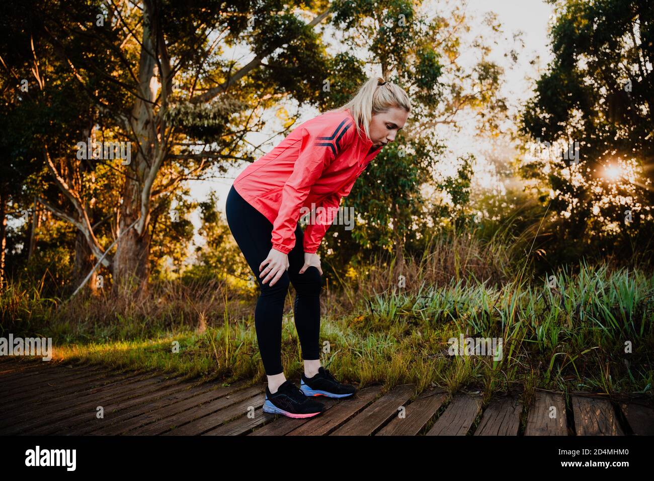 Athletic woman tired from run in the park, bent over breathing heavily ...