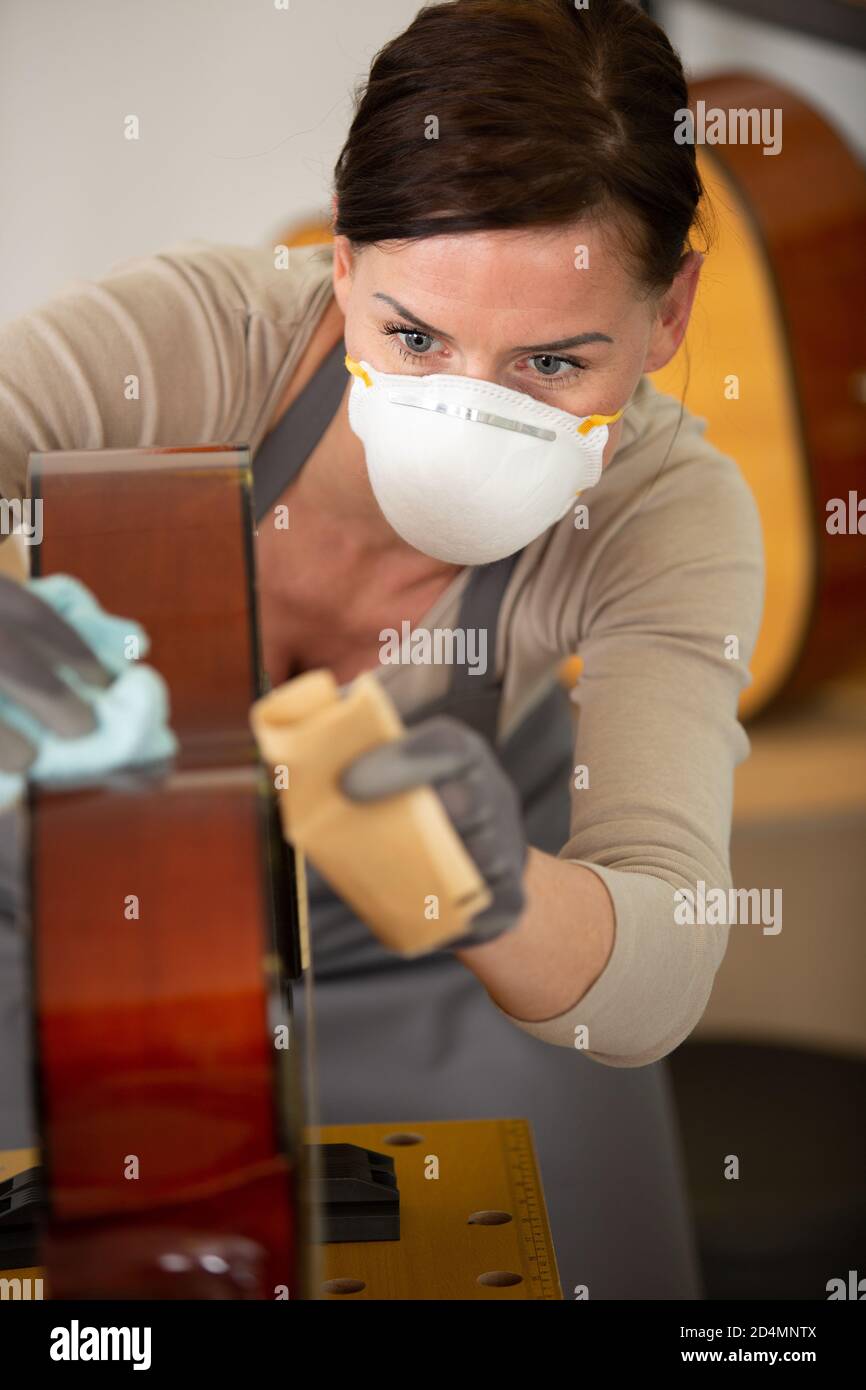 female luthier wearing a mask using sandpaper on a guitar Stock Photo ...