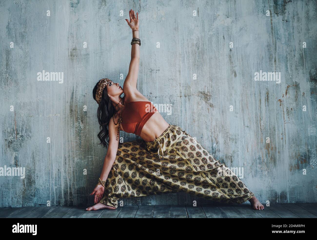 Young beautiful yogi woman in traditional clothing stretching on wall ...