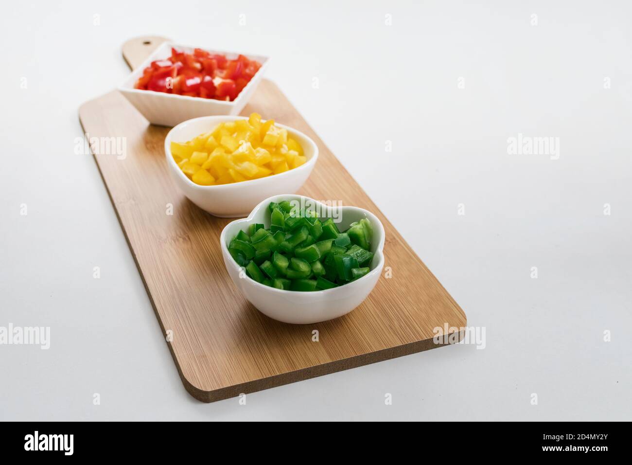 Top view of red, yellow, and peppers cut into cubes in white saucers on ...