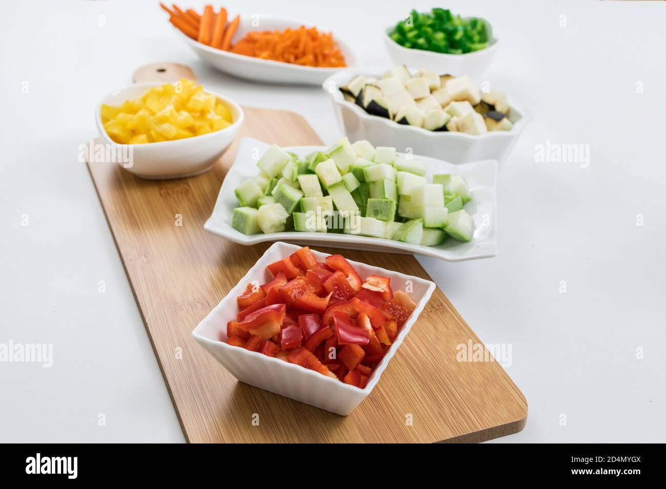 Top view of several vegetables cut into cubes in white saucers with a ...