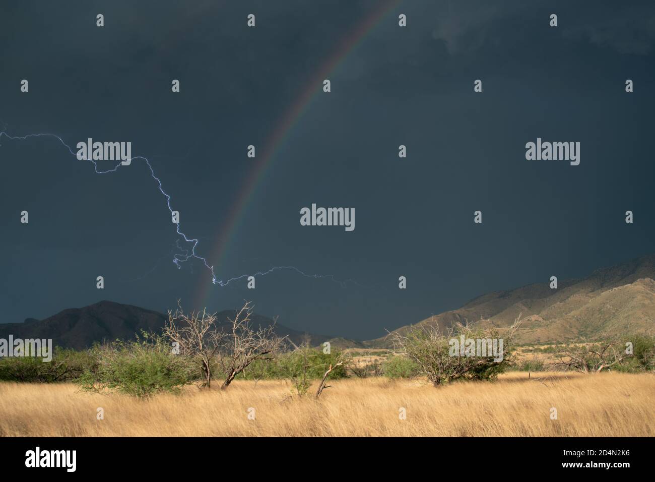 Lightning strike in a rainbow over grasslands and mountains Stock Photo ...