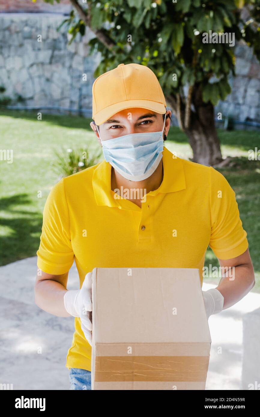 Latin delivery man with mask holding and carrying a cardbox in ...