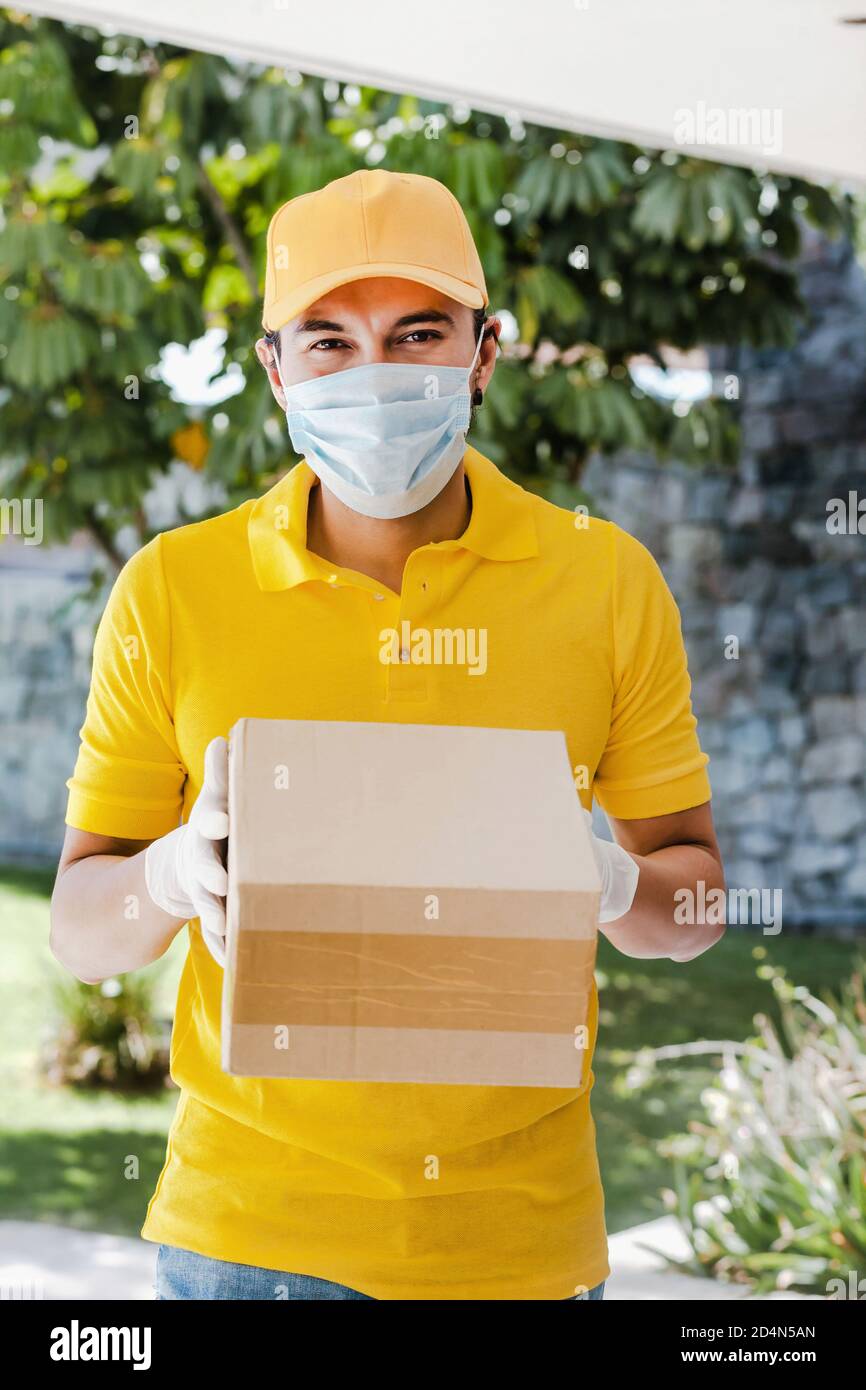 Latin delivery man with mask holding and carrying a cardbox in ...