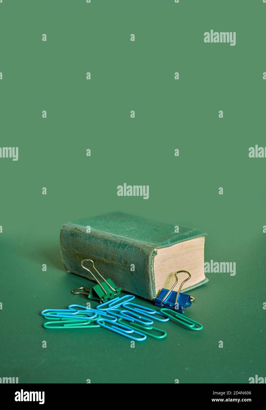 A green-covered book and paper clips lie on a plain green background ...