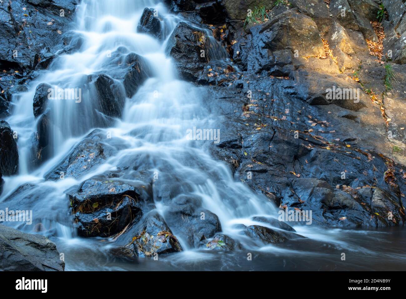 Ethereal long exposure waterfall over black rocks in dappled light ...