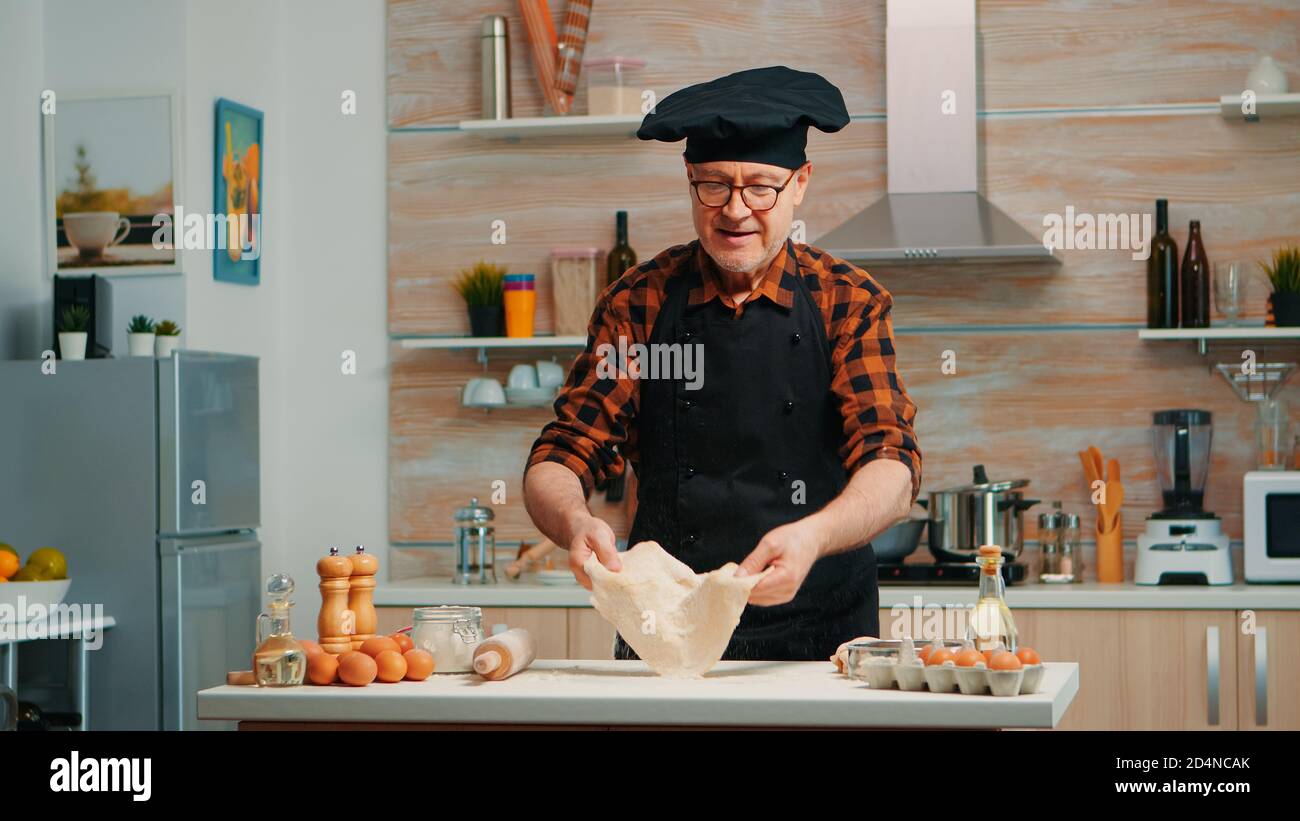 Old man with kitchen apron playing with bread dough at home smiling in ...