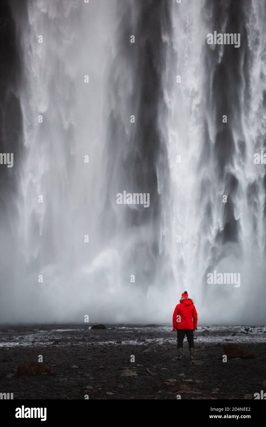 Red clothed man standing in front of water wall of the famous Icelandic ...