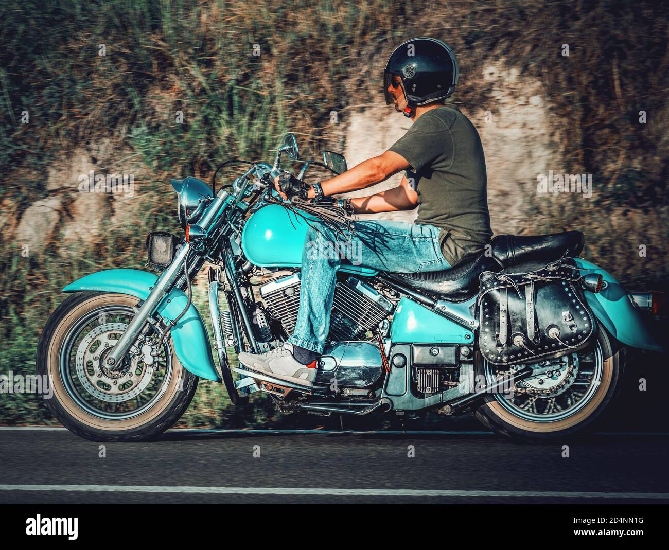 Side view of a biker riding a classic motorcycle on a country road ...
