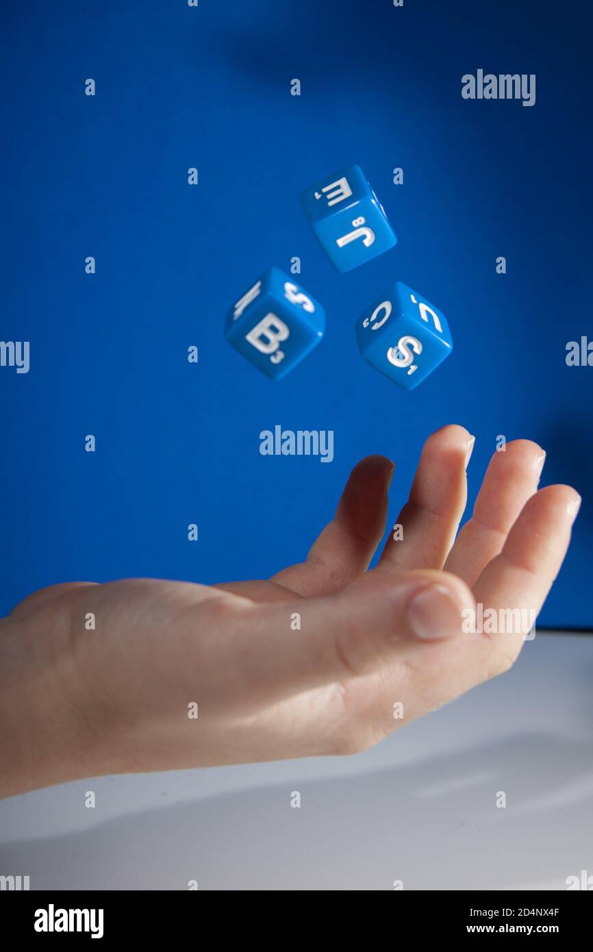 Vertical shot of a hand tossing three letter dice in the air against ...