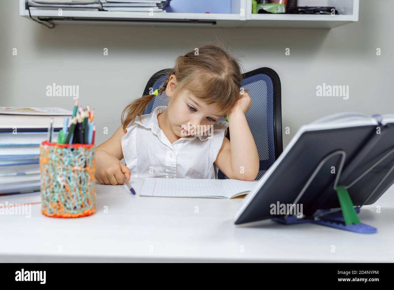 tired little girl sitting at a desk and holding hands to head. baby 4-5 ...
