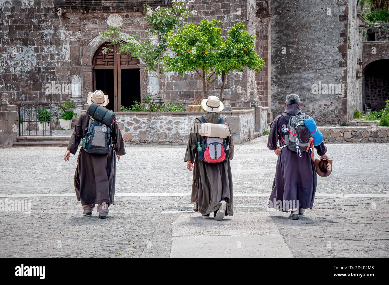 Three monks walk down a street paved with stone towards a historical ...