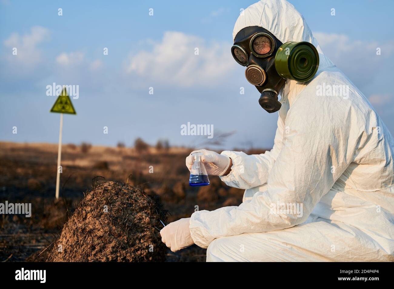 Scientist in protective suit, gas mask holding test tube with blue ...