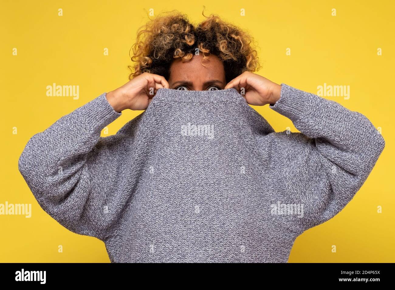 Displeased young afraid woman wearing a high neck sweater, hiding form ...