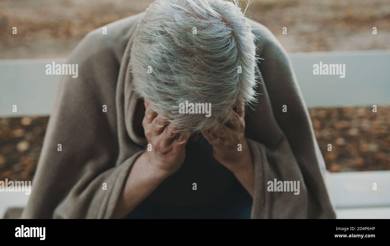 Poor sad homeless man crying on the bench covered with blanket. Social ...