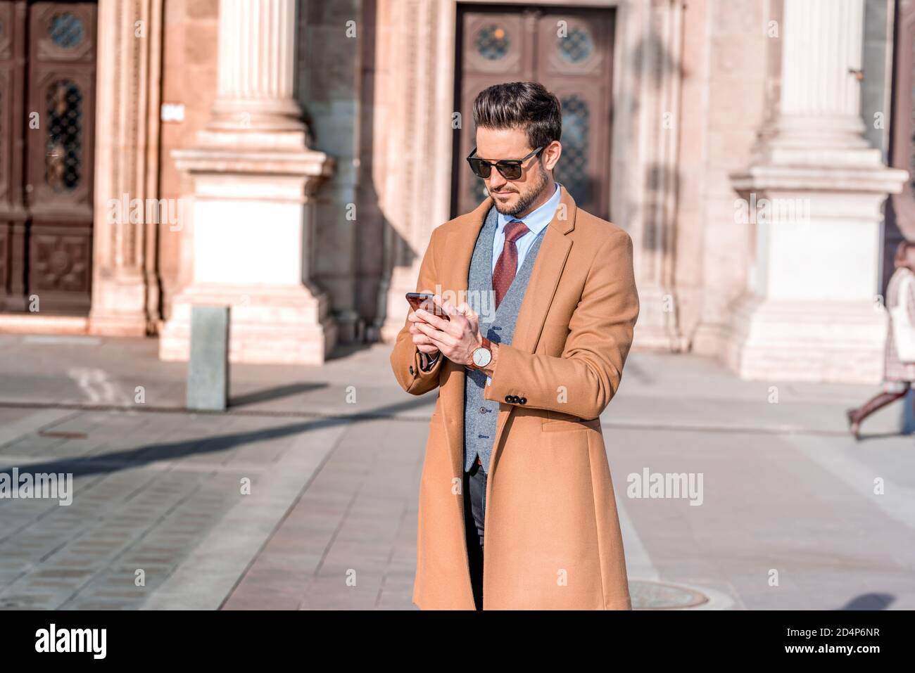 A handsome elegant man standing on a square and using his smartphone on ...