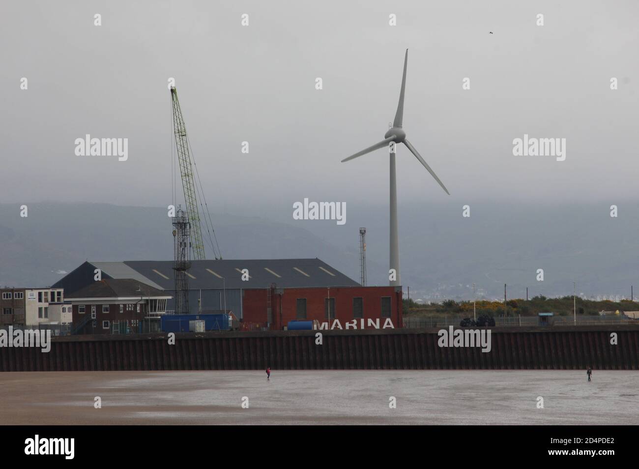 A photograph of industrial buildings and a wind turbine generator next ...