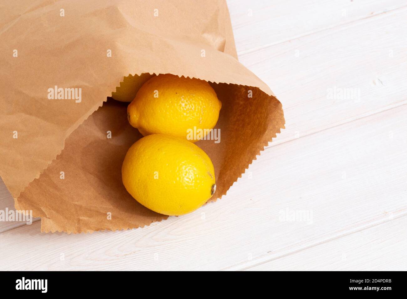 Lemons in a brown paper bag on a white wood background. Environmentally ...