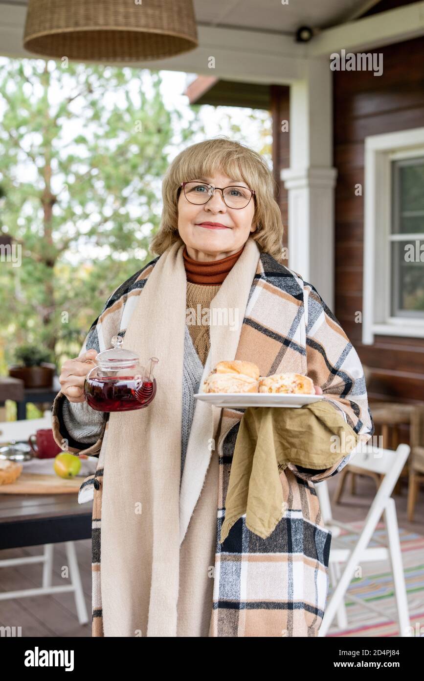 Happy mature blond female wrapped in checkered woolen plaid holding ...