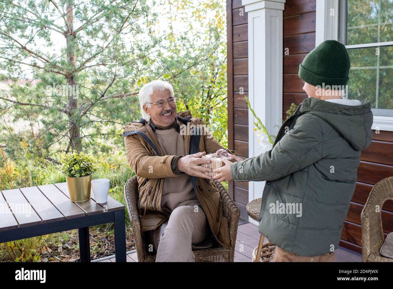 Joyful grandfather passing birthday surprise in giftbox to his grandson ...