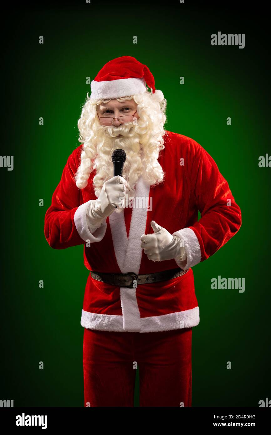 Male actor in a costume of Santa Claus holds a microphone in his hands ...