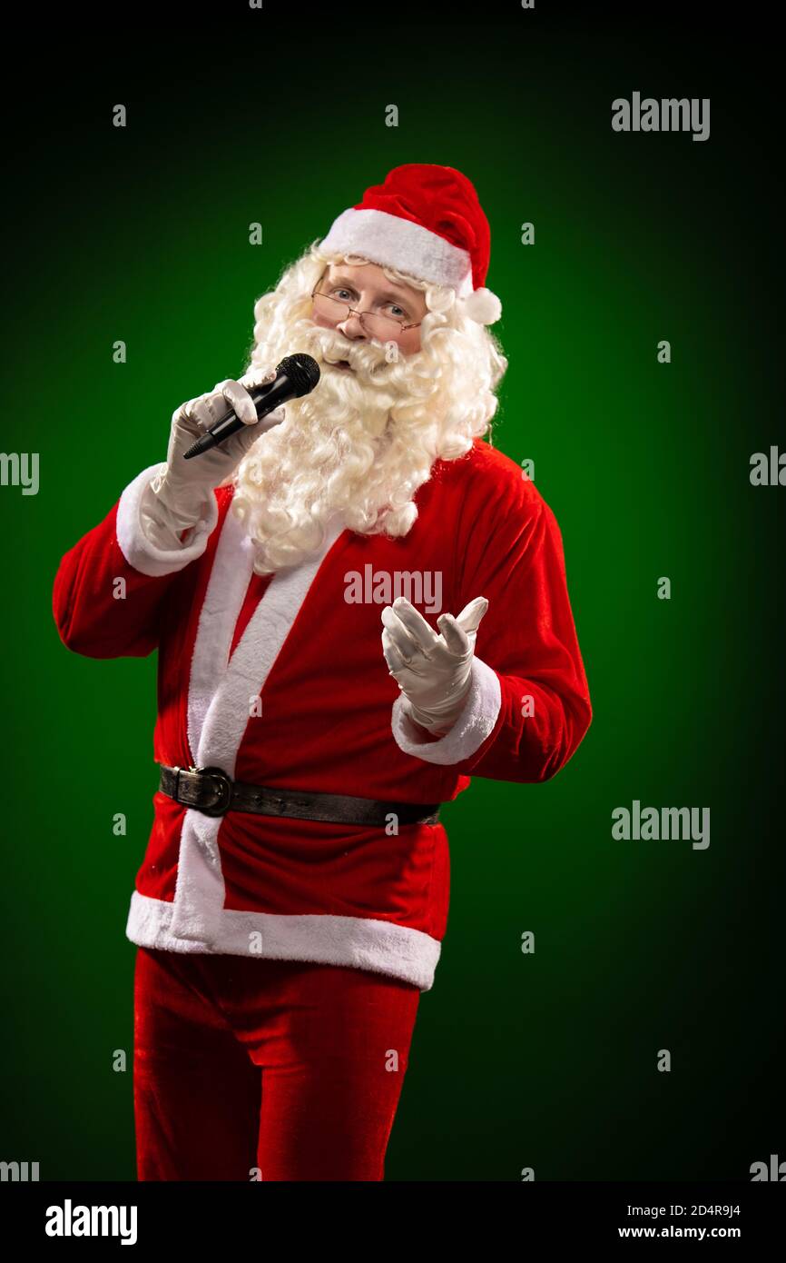 Male actor in a costume of Santa Claus holds a microphone in his hands ...