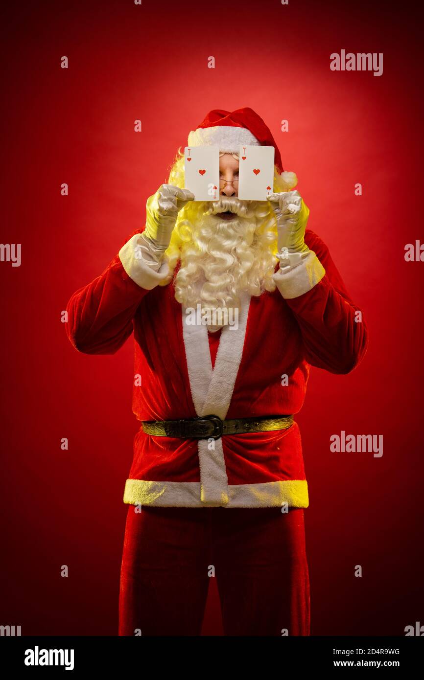 Santa Claus holds playing cards in his hands and poses on a dark red ...
