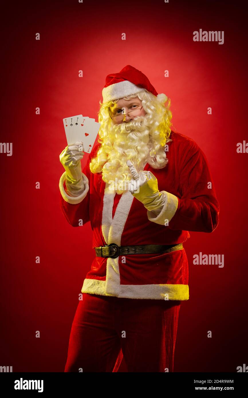 Santa Claus holds playing cards in his hands and poses on a dark red ...