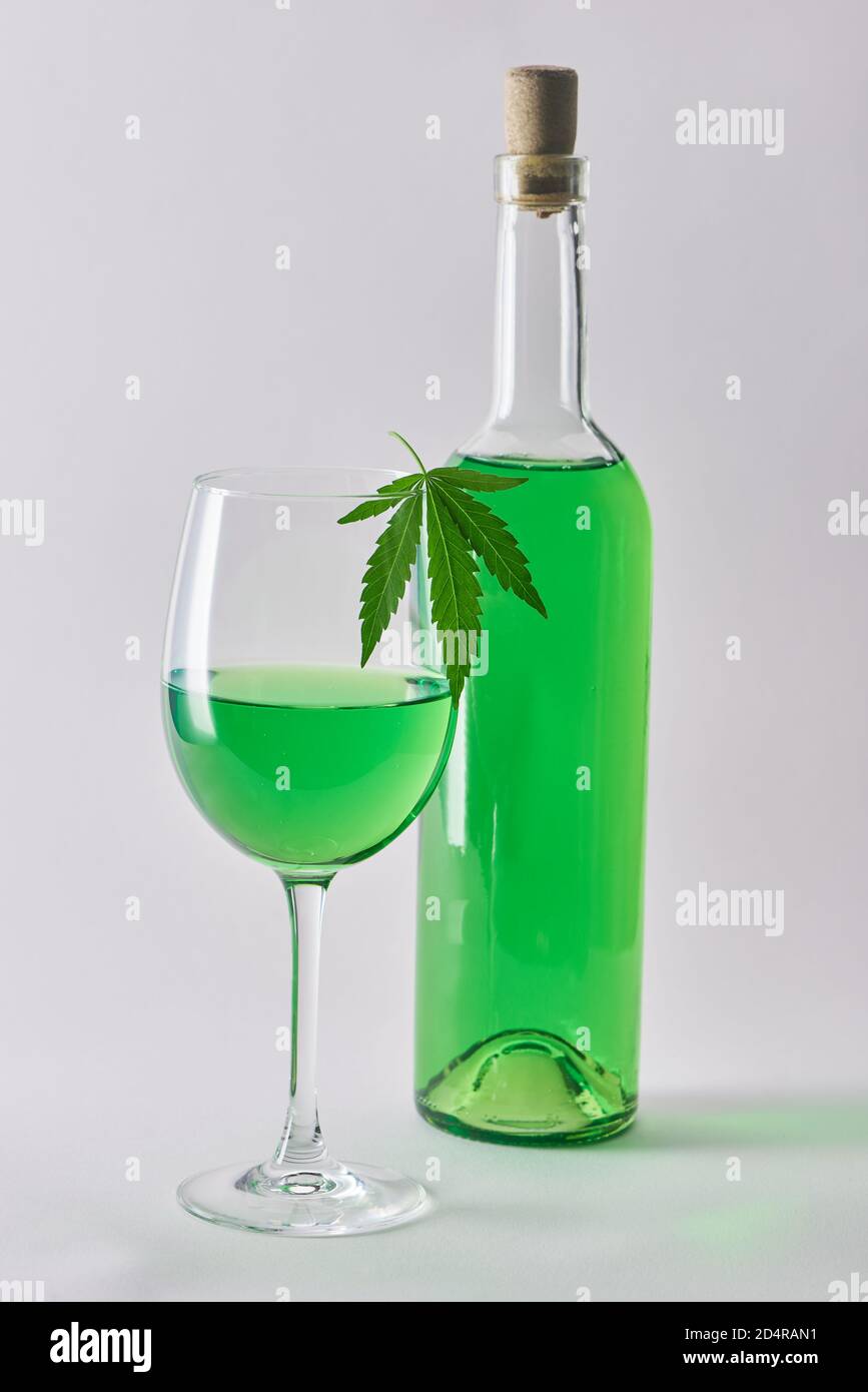 A glass and a bottle of green hemp-infused wine on white background ...