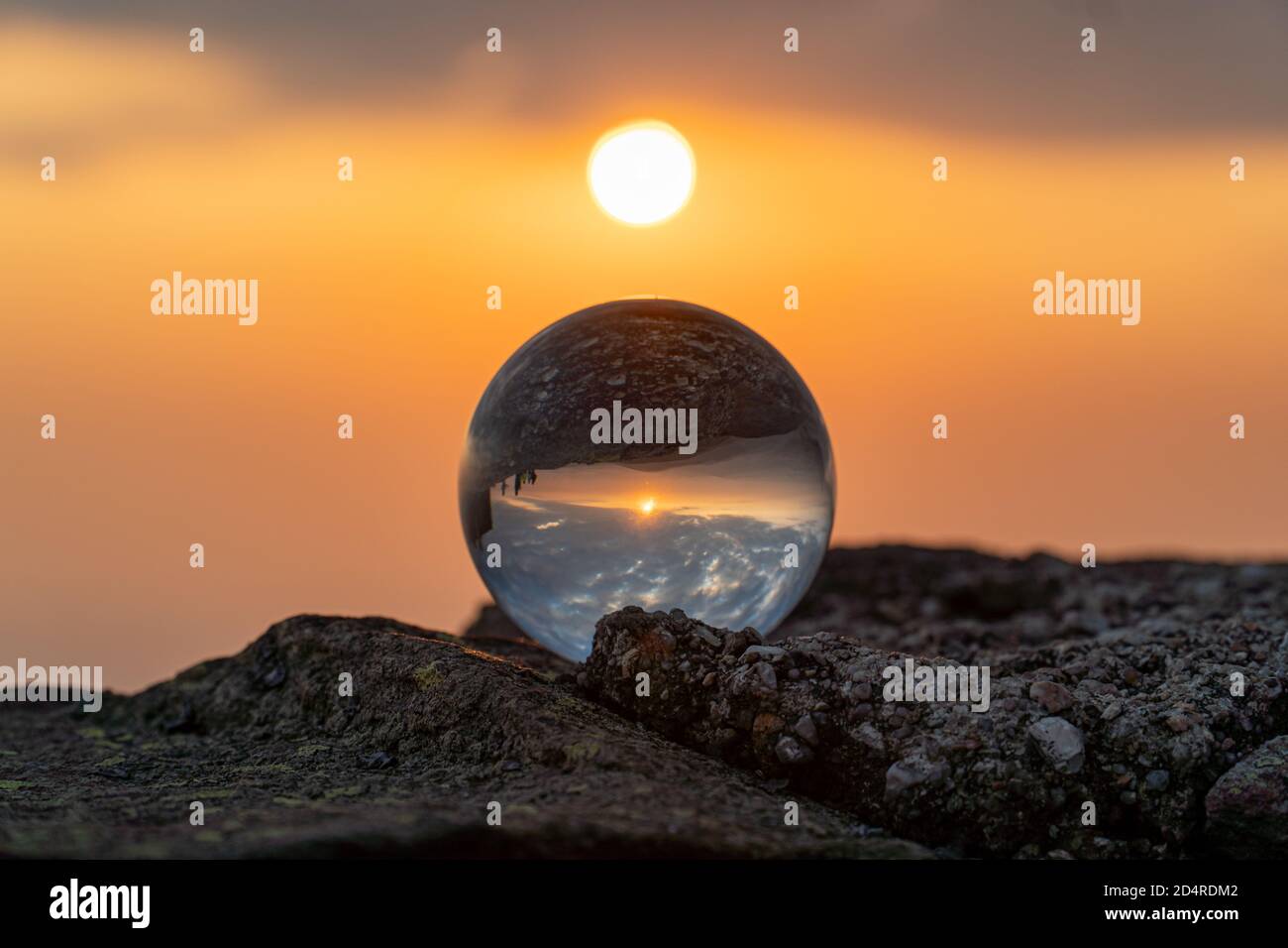 A glass ball placed on a rock, you can see the sunrise in the ...