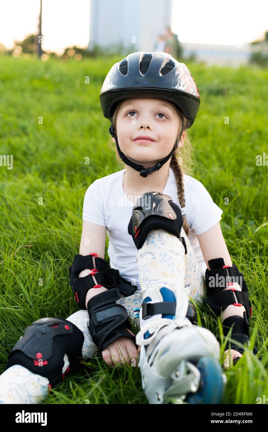 Little girl in protective equipment and rollers. sitting on the grass a ...