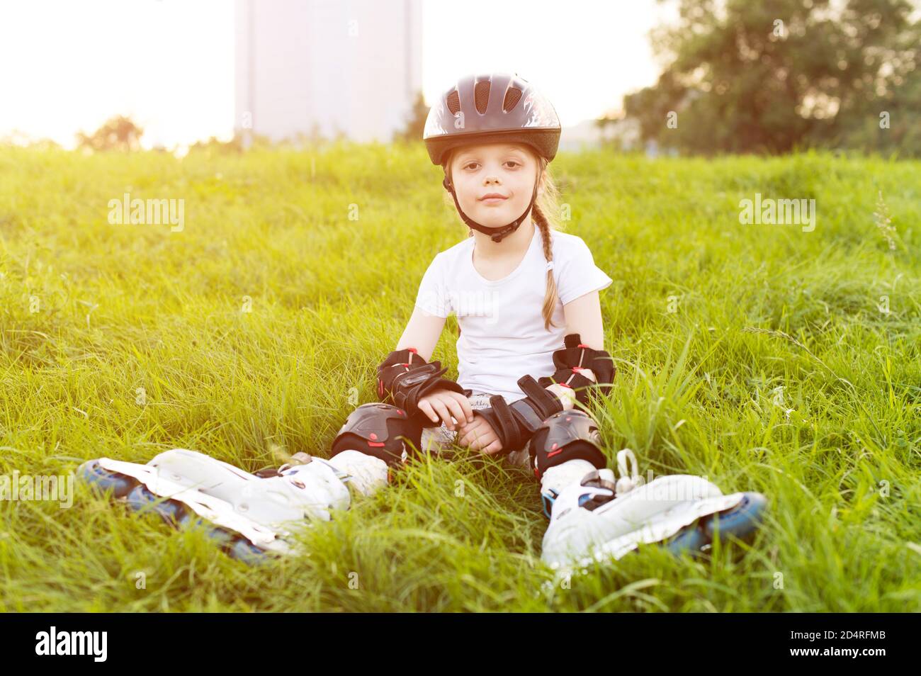 Little pretty girl on roller skates in helmet sitting on the grass at ...