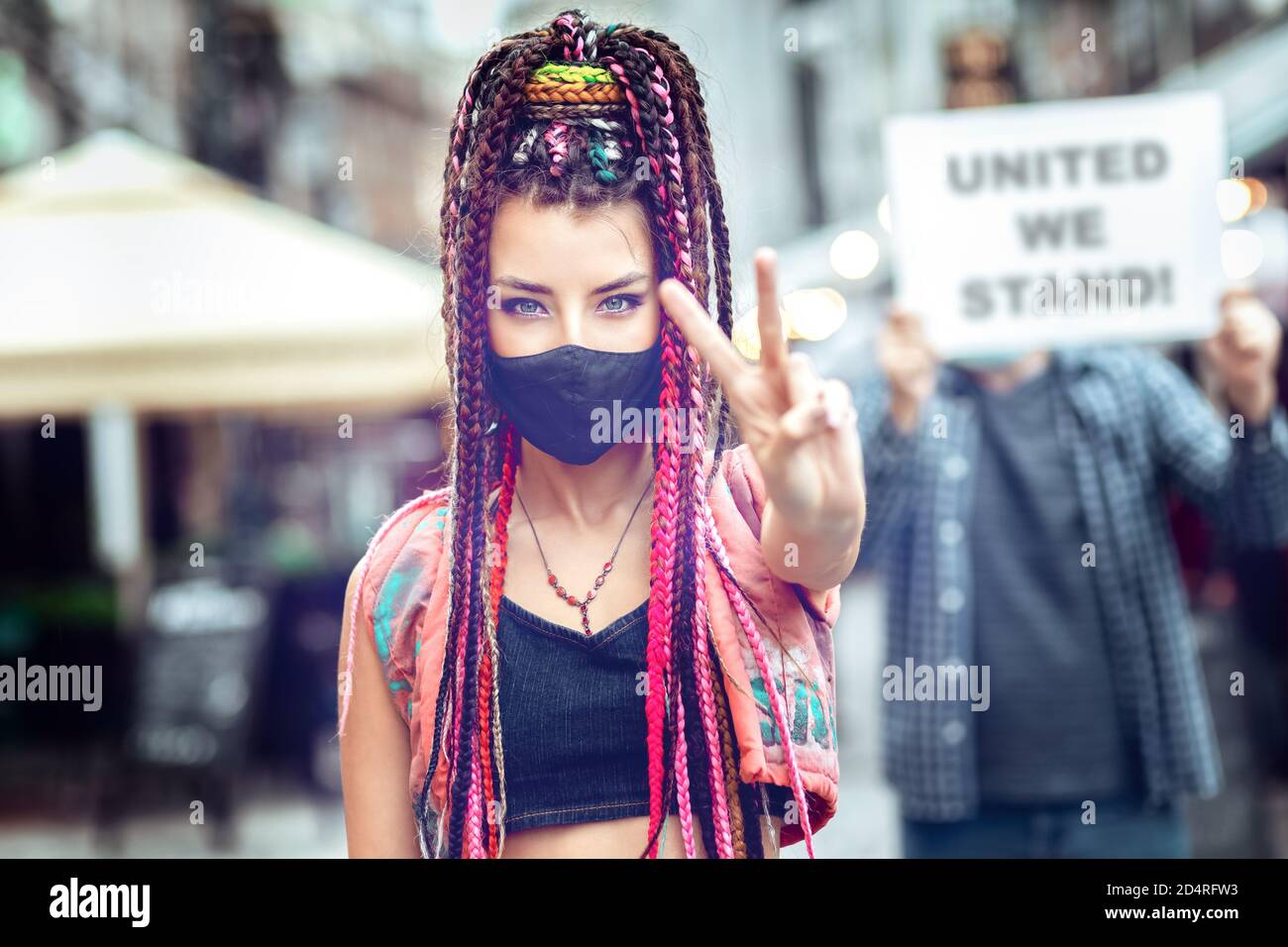 Mixed race woman with face mask showing peace sign during street ...