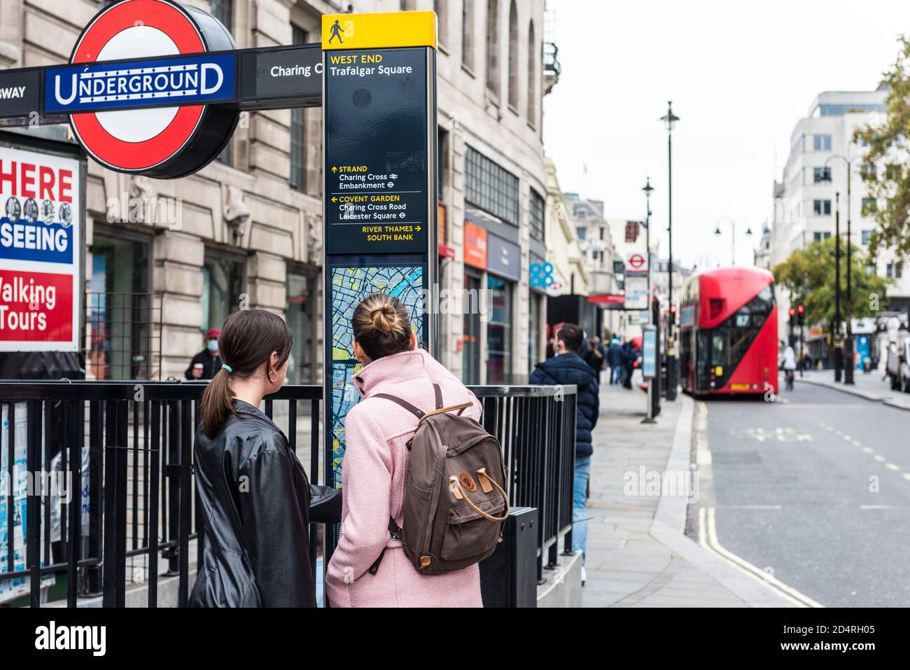 Two women looking at physical Map on roadside pillar in London ...