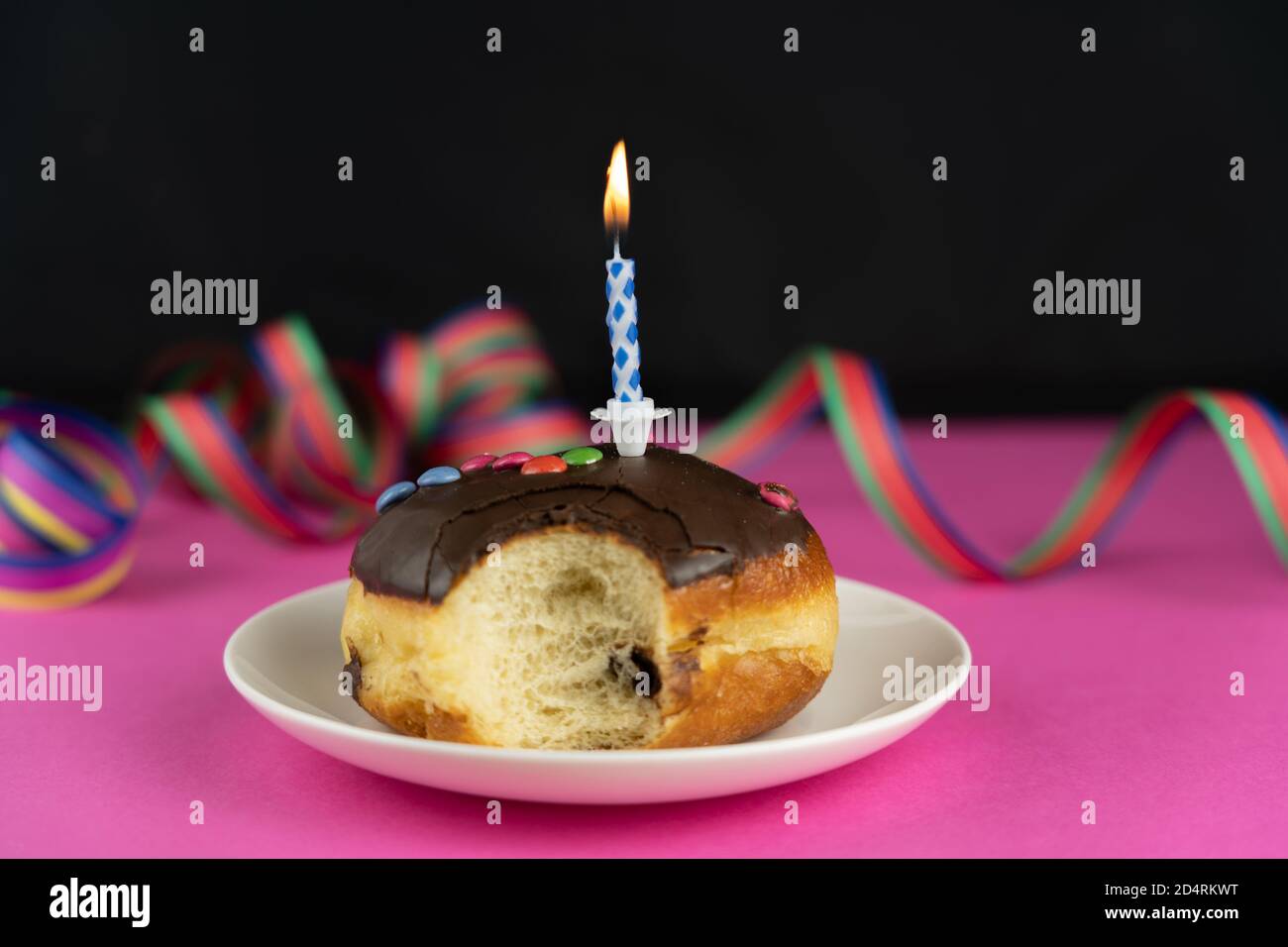 Sweet donut with one burning candle on pink and black background Stock Photo - Alamy