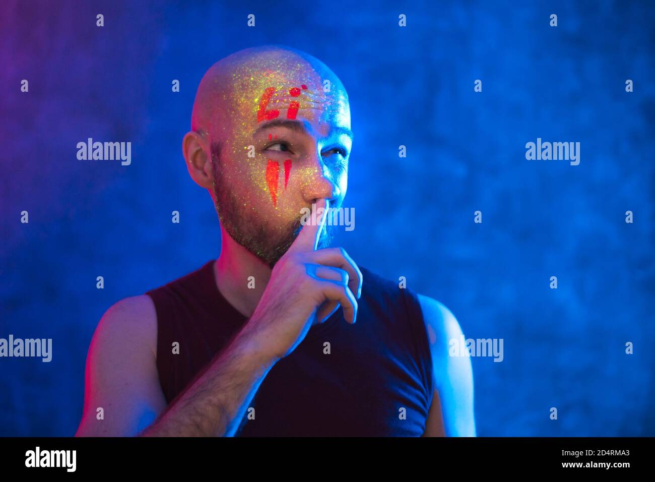 Stylish bald man with drawing face picks nose. Fluorescent paint in ...