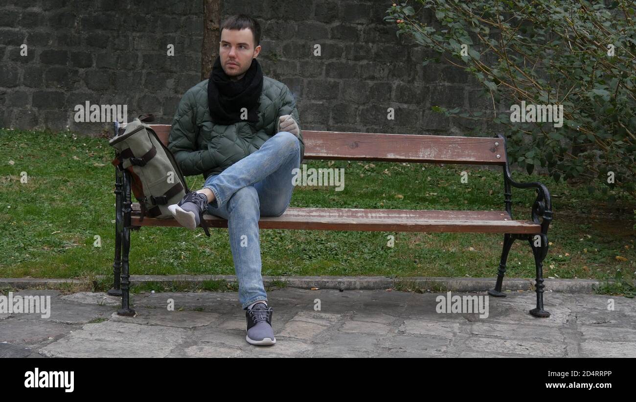 Man smoking while sitting on bench outdoors Stock Photo - Alamy