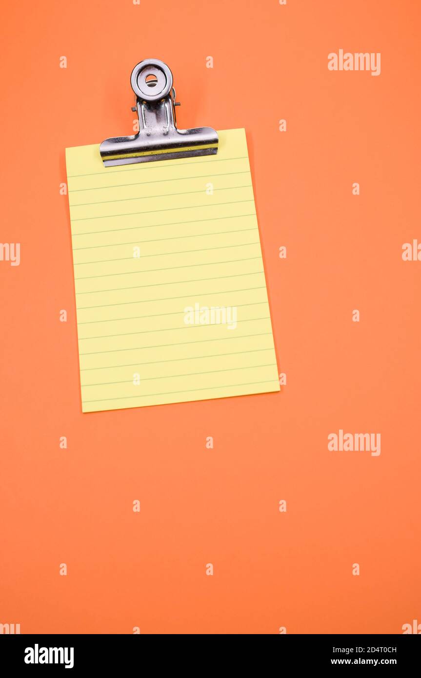 Vertical shot of a notepad and a paper clipper isolated on an orange ...