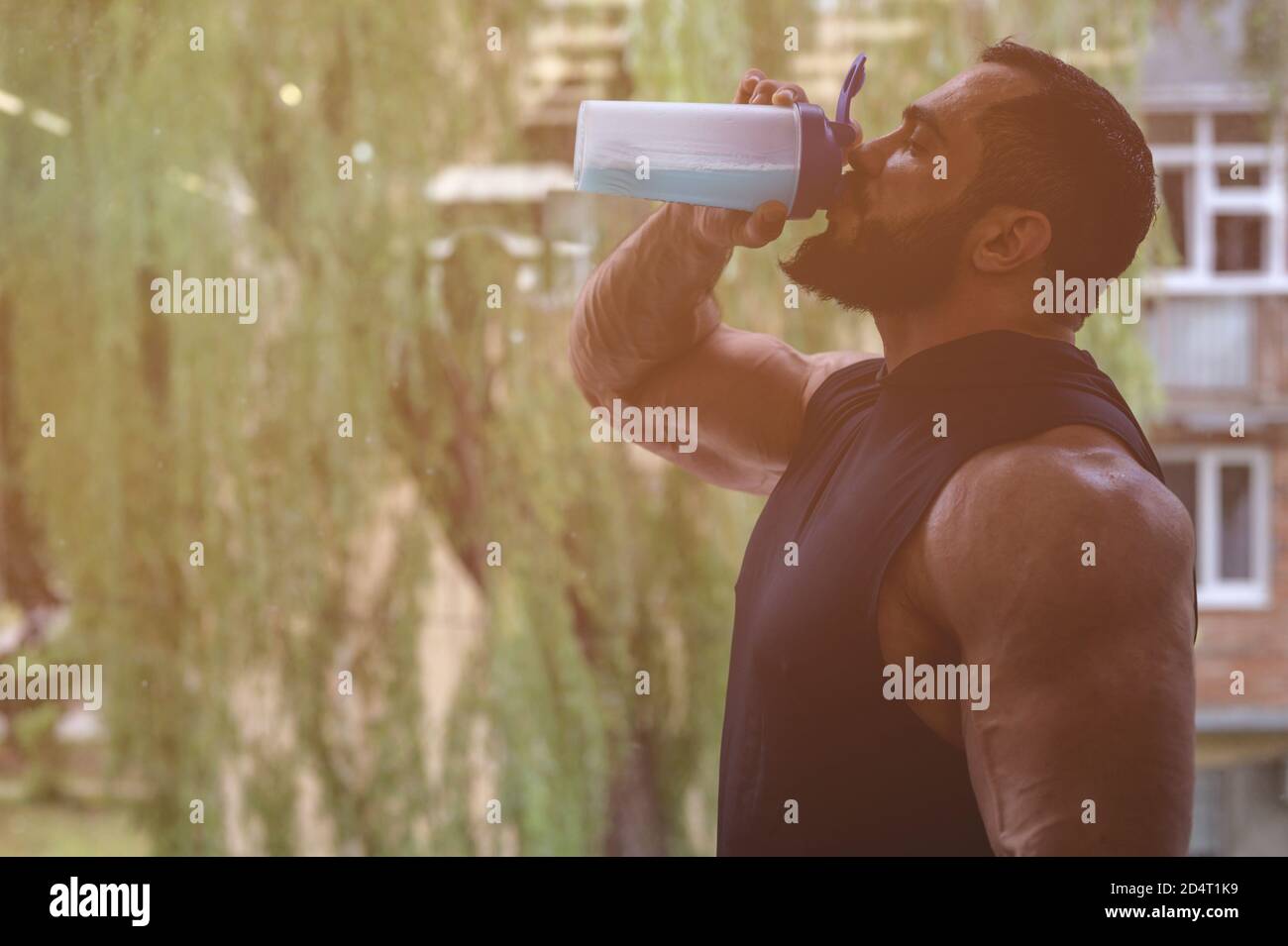 strong young athlete drinking energy drink during from bottle shaker ...