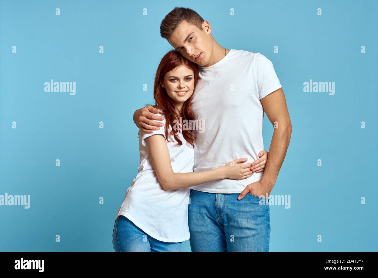 enamored man and woman in jeans and a T-shirt on a blue background hug ...