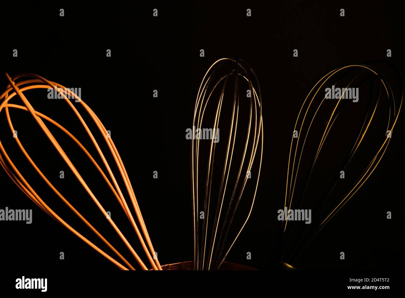 View on three isolated shiny wire whisk loops, black background (focus ...