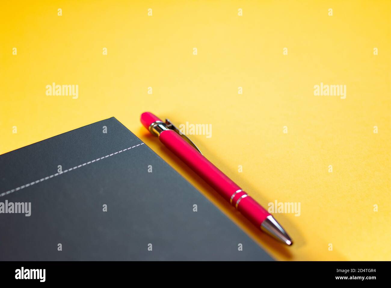 Closeup shot of a notebook and a pen isolated on a yellow background ...