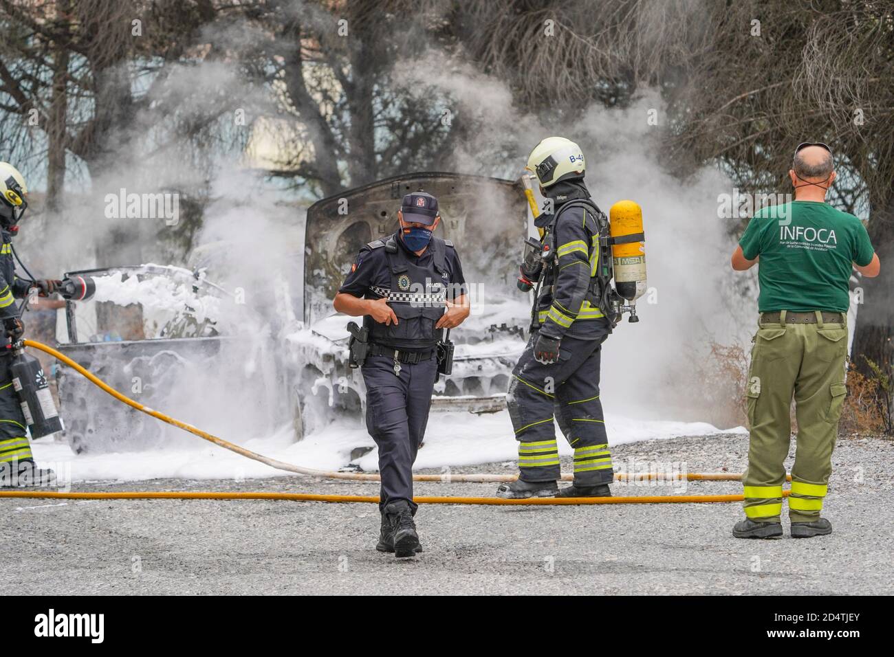 Fire fighters extinguish a fire with white foam on a burning car in a ...