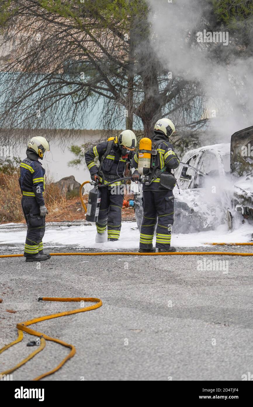 Fire fighters extinguish a fire on a burning car in a forest area ...